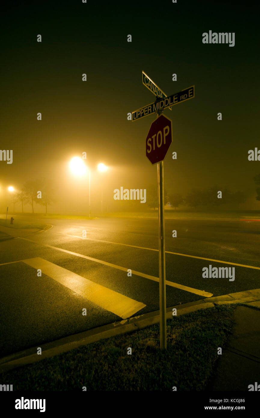 Stop sign at crossroads lit by street lights at night Stock Photo - Alamy