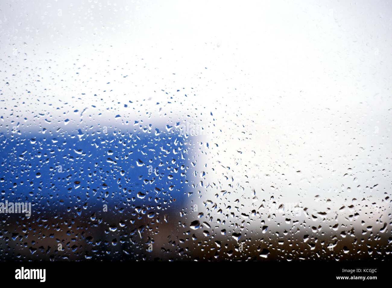 Raindrop condensation on a window interior with a defocused blue roofed ...