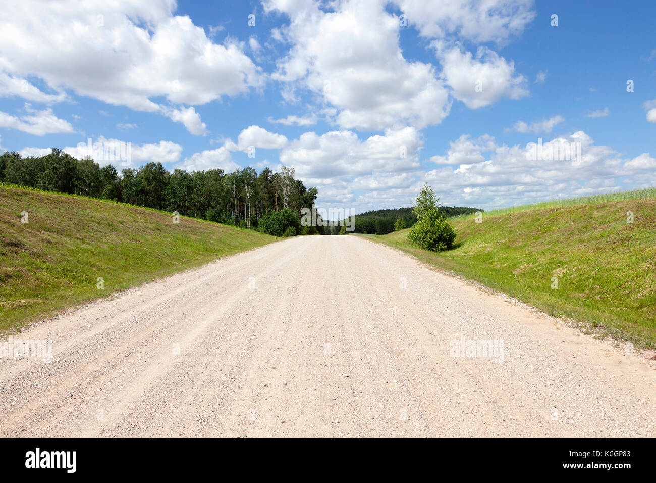 A wide country road against a blue sky with clouds. On the sides of the ...