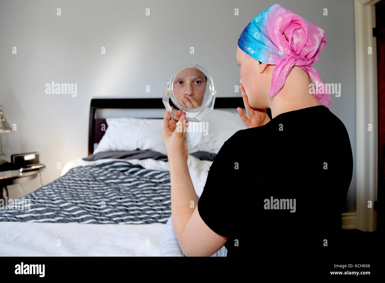 Young cancer patient in a headscarf looks shocked at reflection in ...