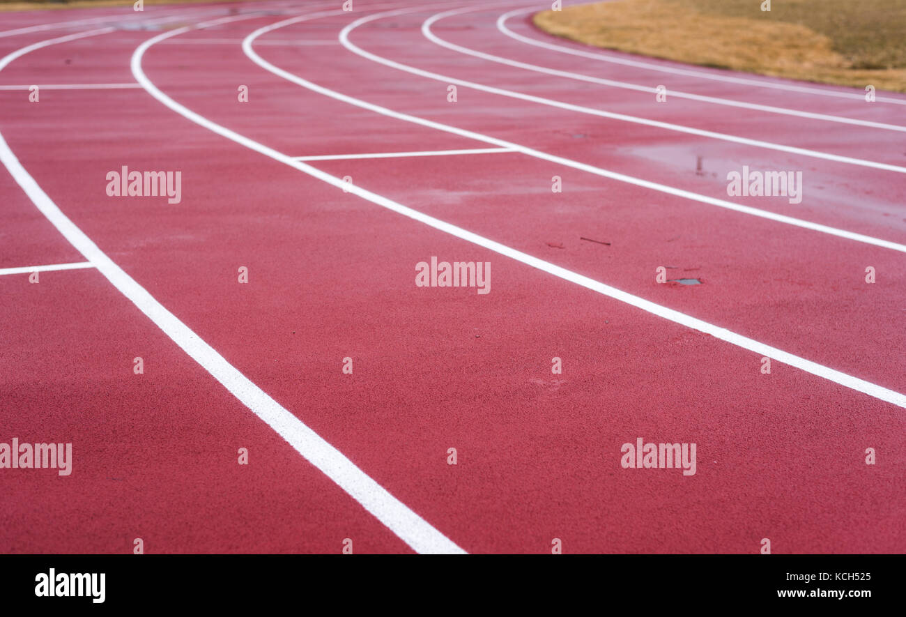 White lines mark the lanes on a wet worn red running track Stock Photo ...