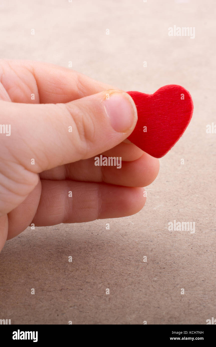 Little red color heart shape in hand on light brown background Stock ...