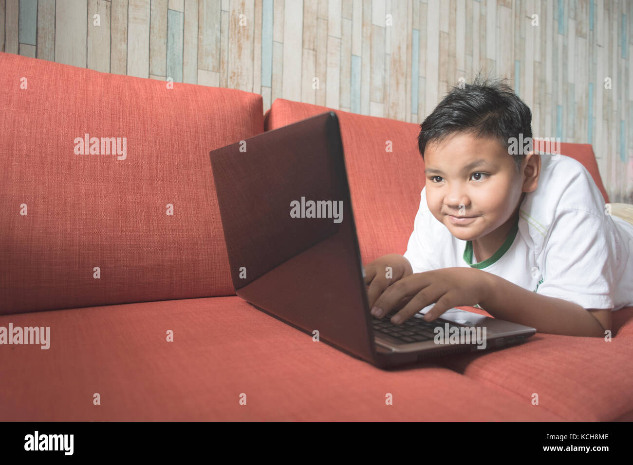 young asian boy using laptop computer on a sofa at home. boy relaxing ...