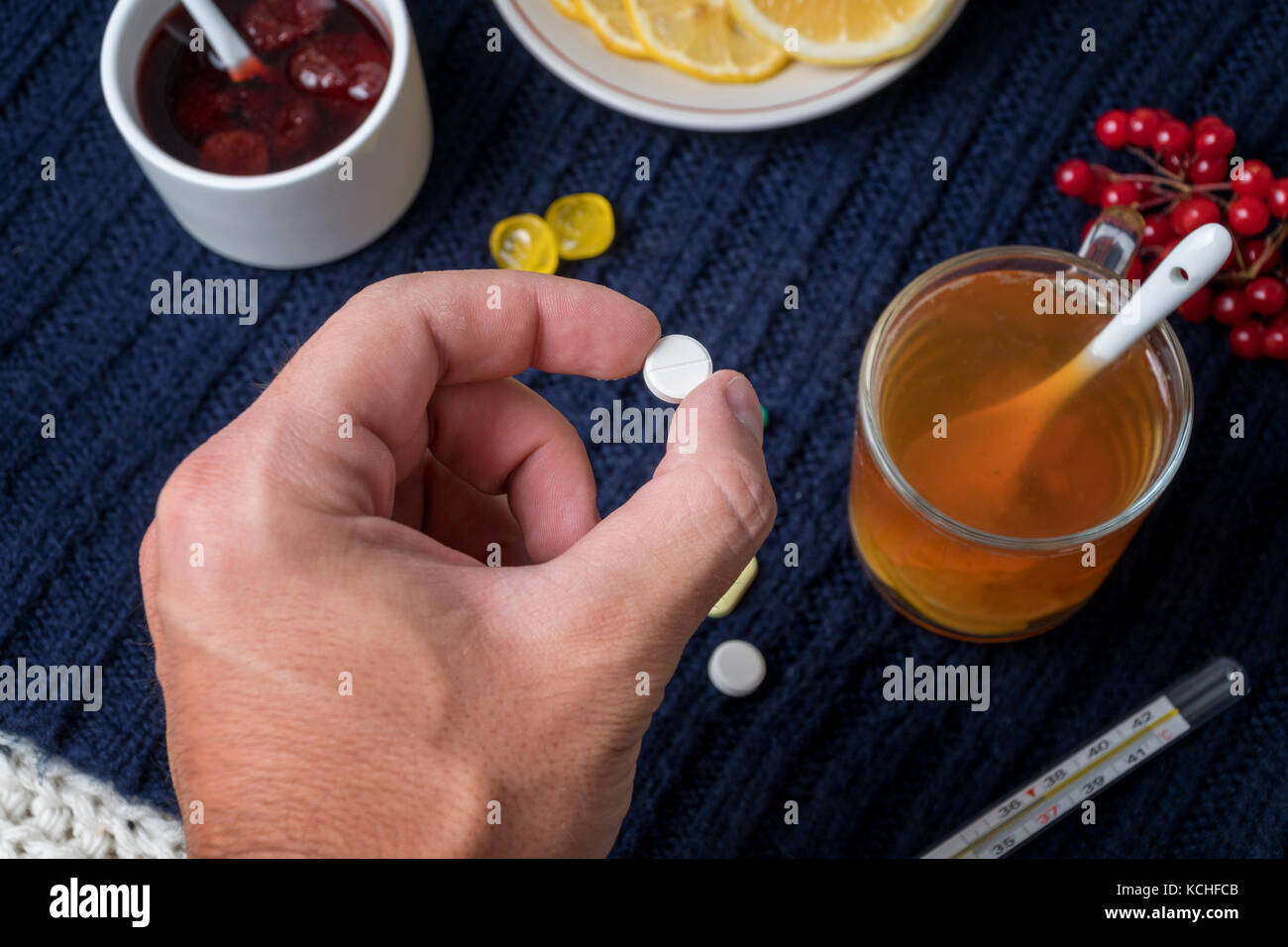 A man's hand holds a pill. Still life of tea with lemon, tablets and ...