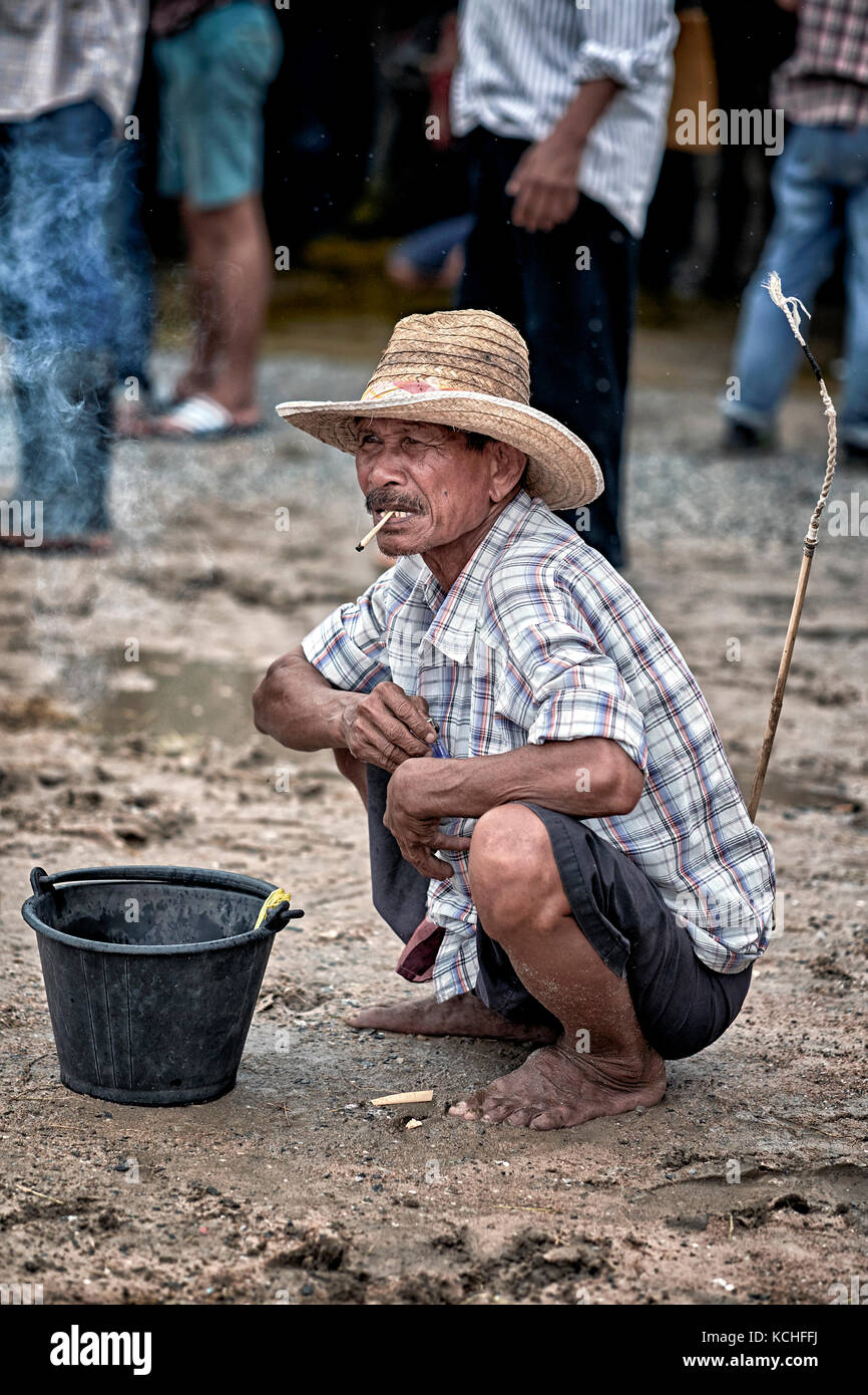 Elderly Thailand man squatting and smoking a cigarette. Southeast Asia ...