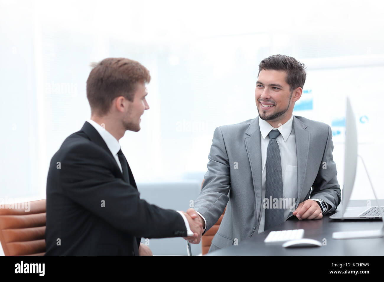 handshake of business partners sitting at a Desk Stock Photo - Alamy