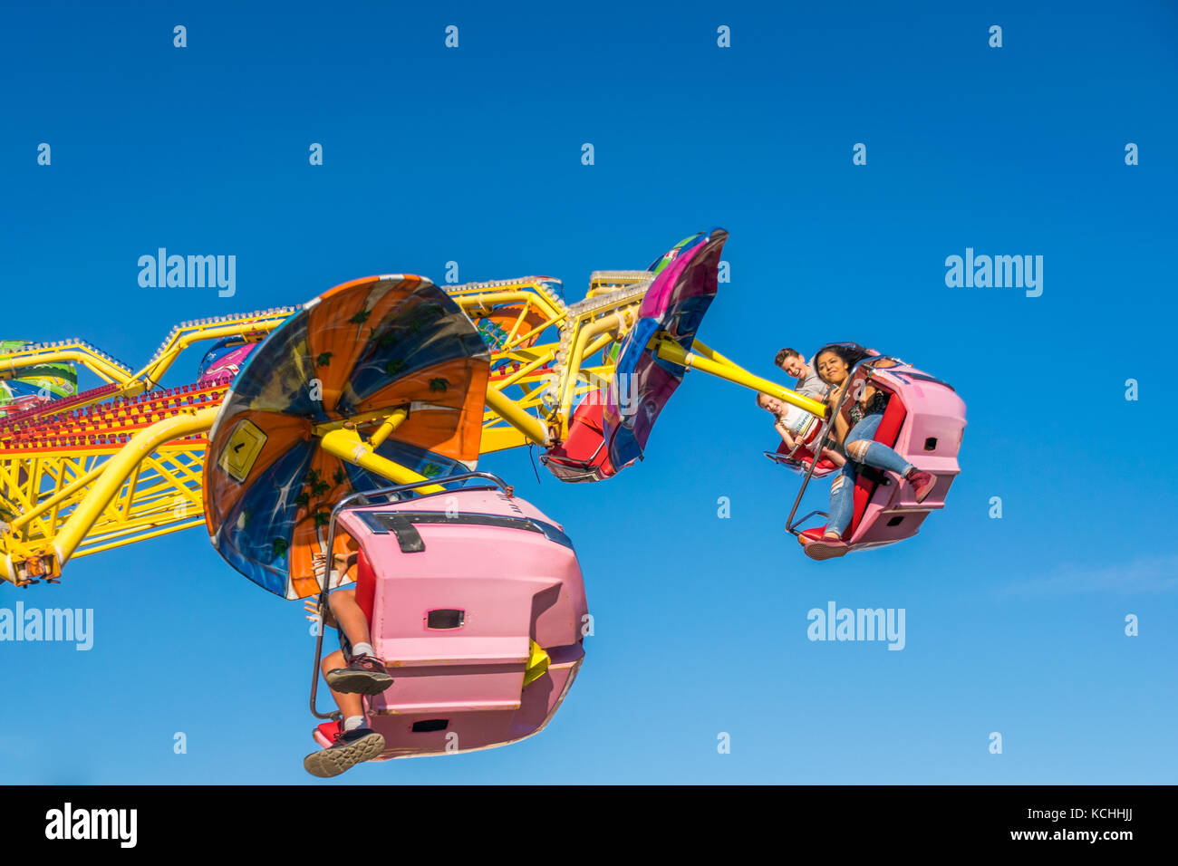 Young people enjoy a summer fairground ride on umbrellas under blue sky ...
