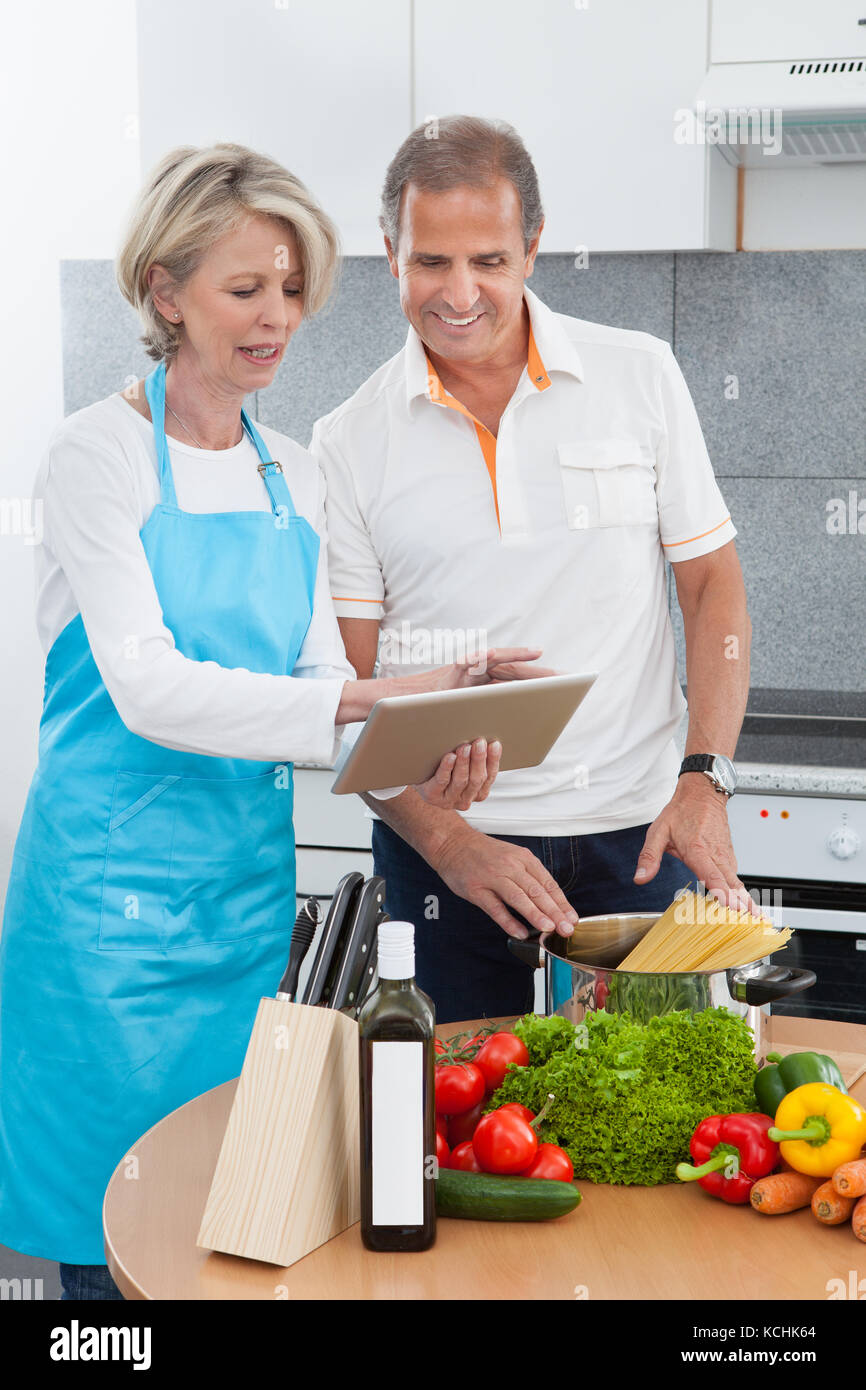 Mature Man And Woman Looking At Recipe Tablet While Cooking In Kitchen ...