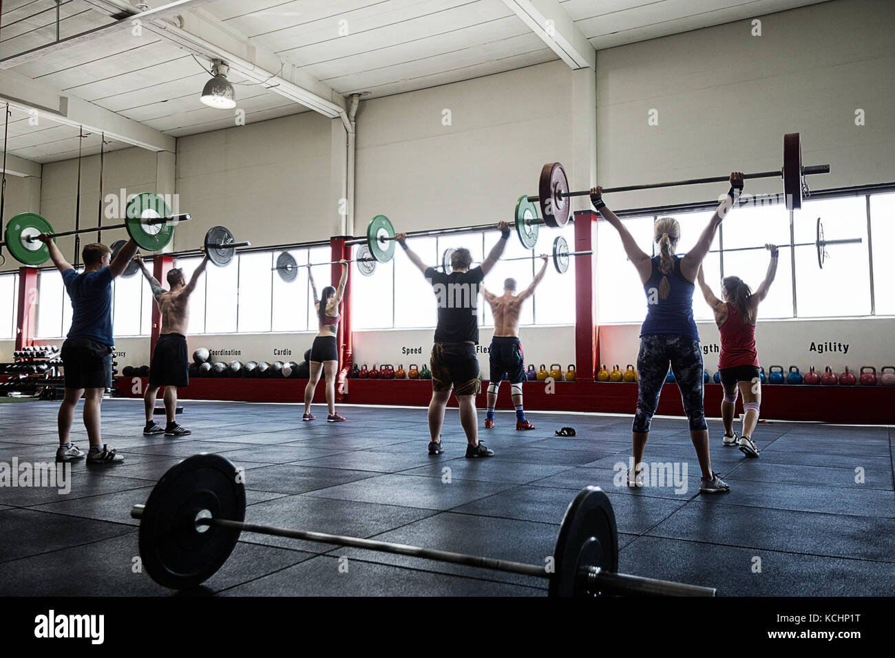 Full length rear view of male and female clients lifting barbells in ...