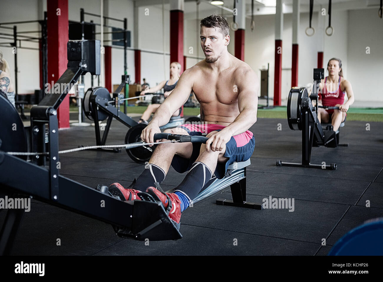 Full length of young shirtless man using rowing machine in gymnasium ...