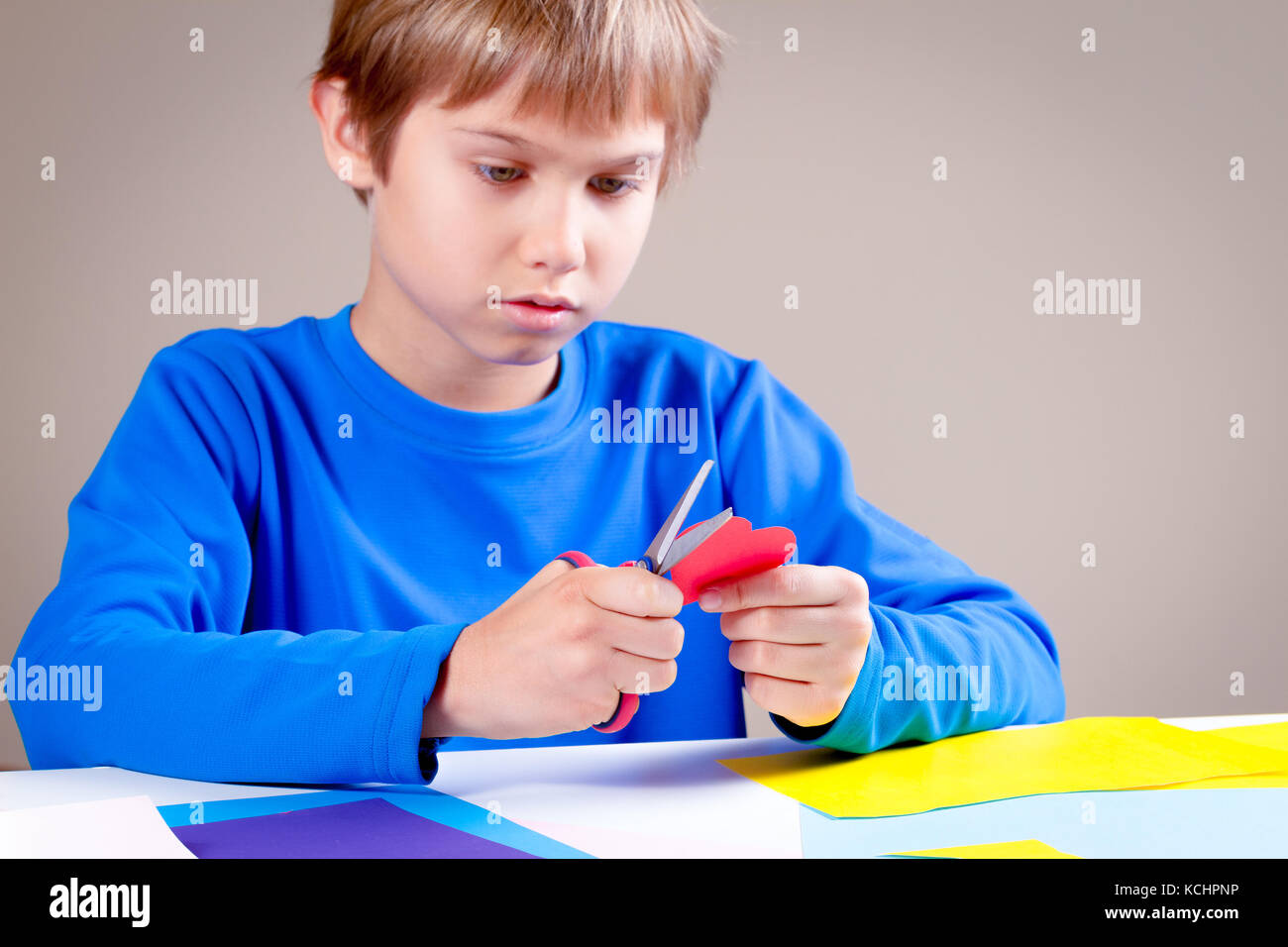 Boy cutting colored paper with scissors at the table Stock Photo - Alamy