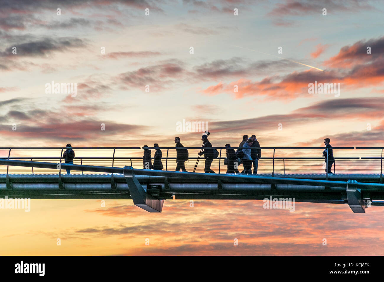 Pedestrian people crossing the Millennium Bridge in London at sunset ...