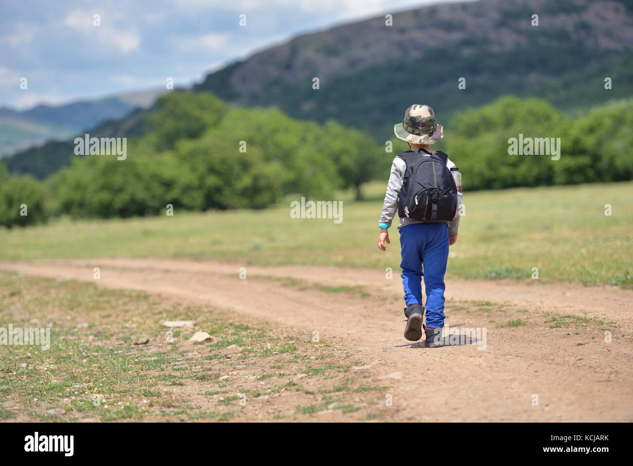 Cute child boy with backpack walking on a little path in mountains ...