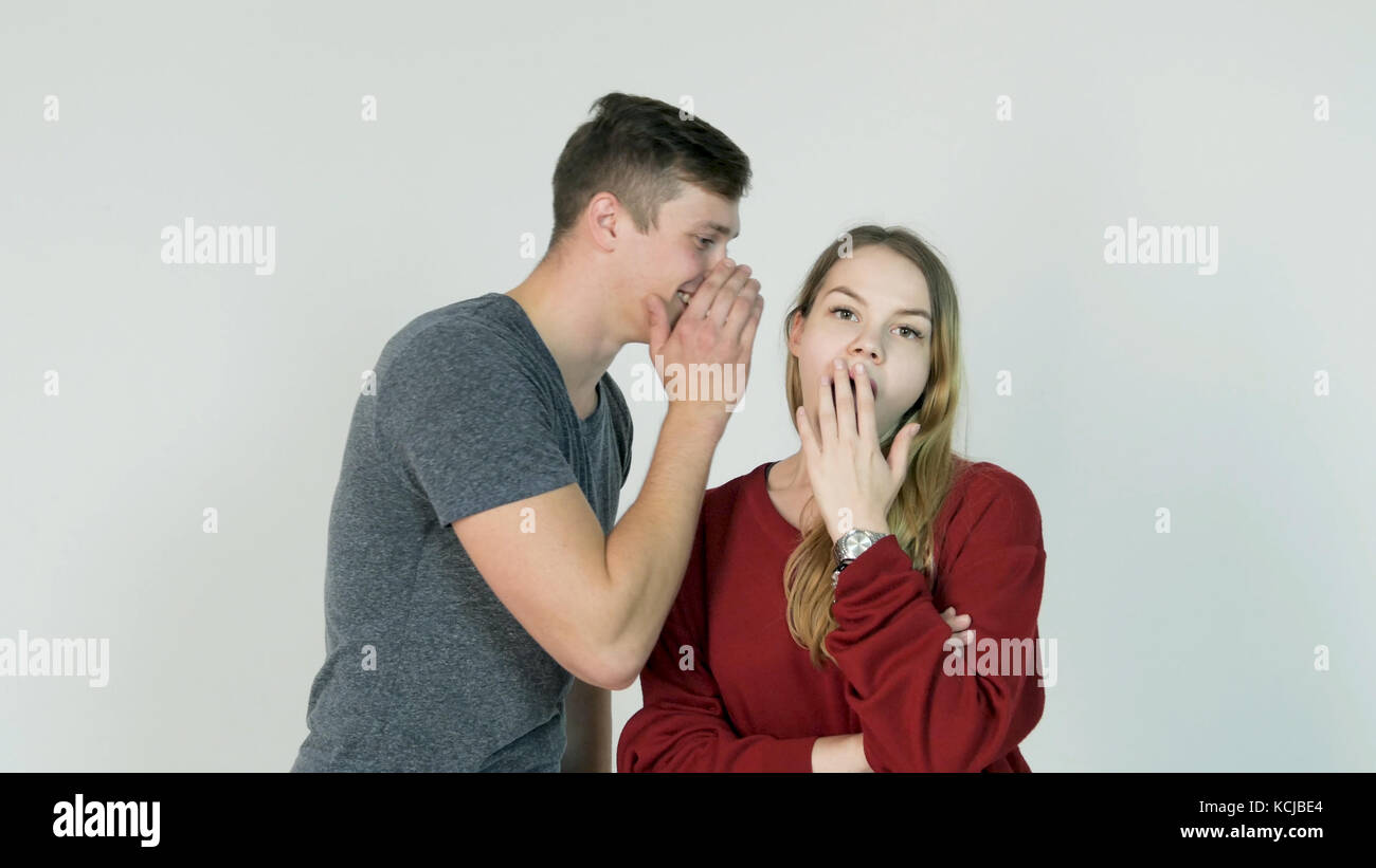 Pretty girl whispering secret in ear of her laughing friend on white ...