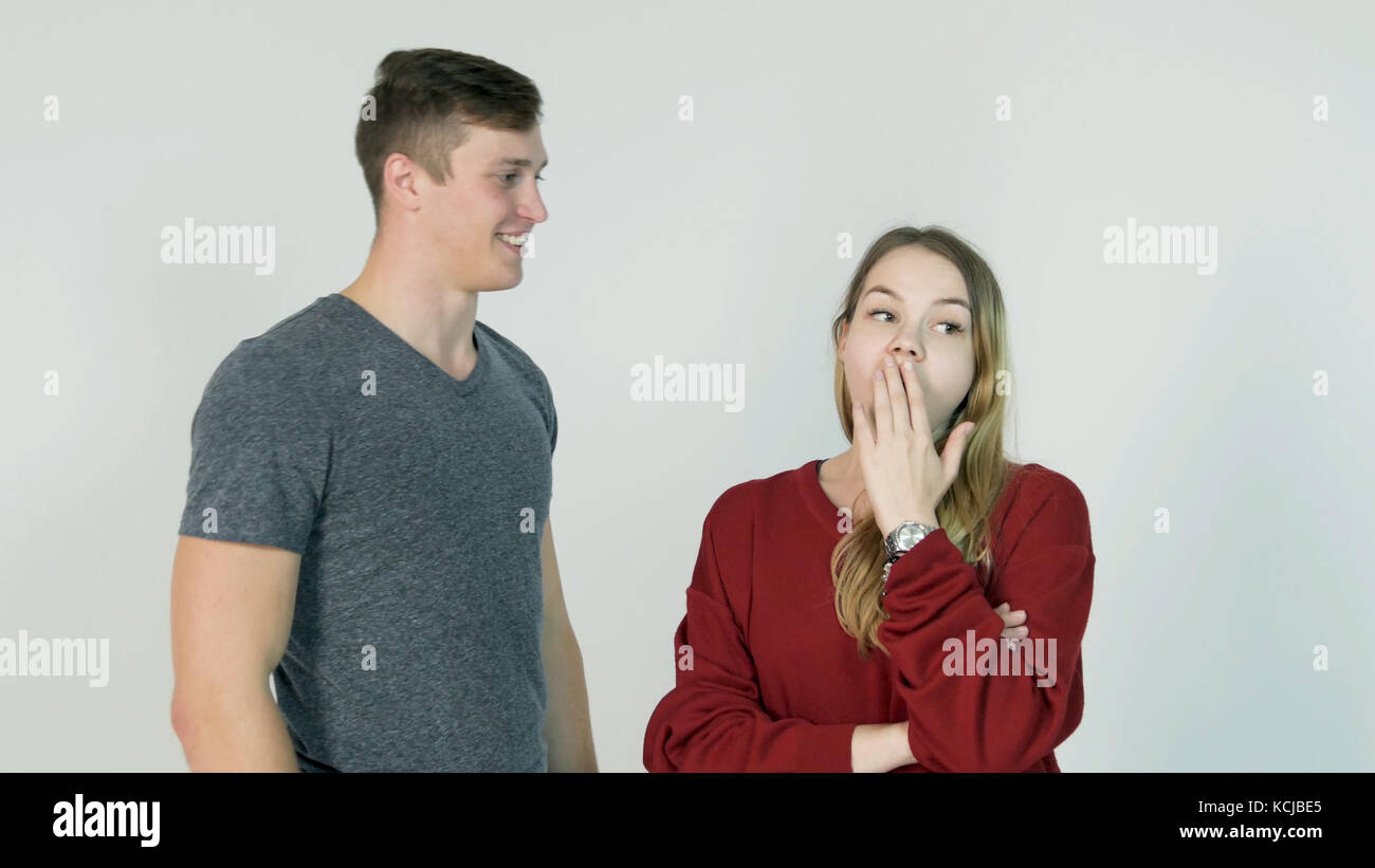 Pretty girl whispering secret in ear of her laughing friend on white ...