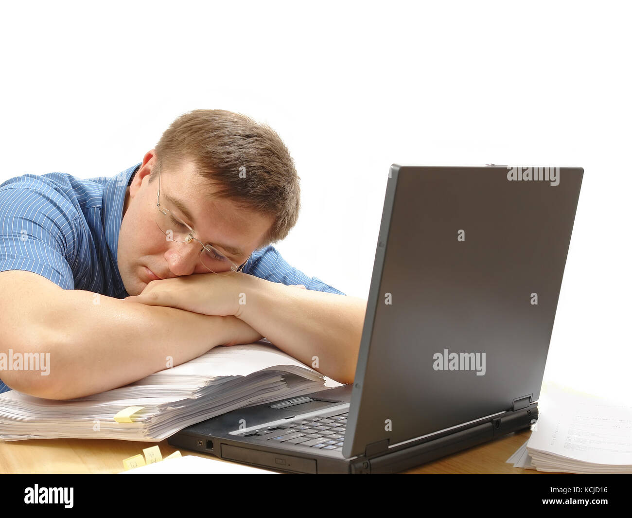 Young man sleeping behind the desk with laptop on piles of documents ...