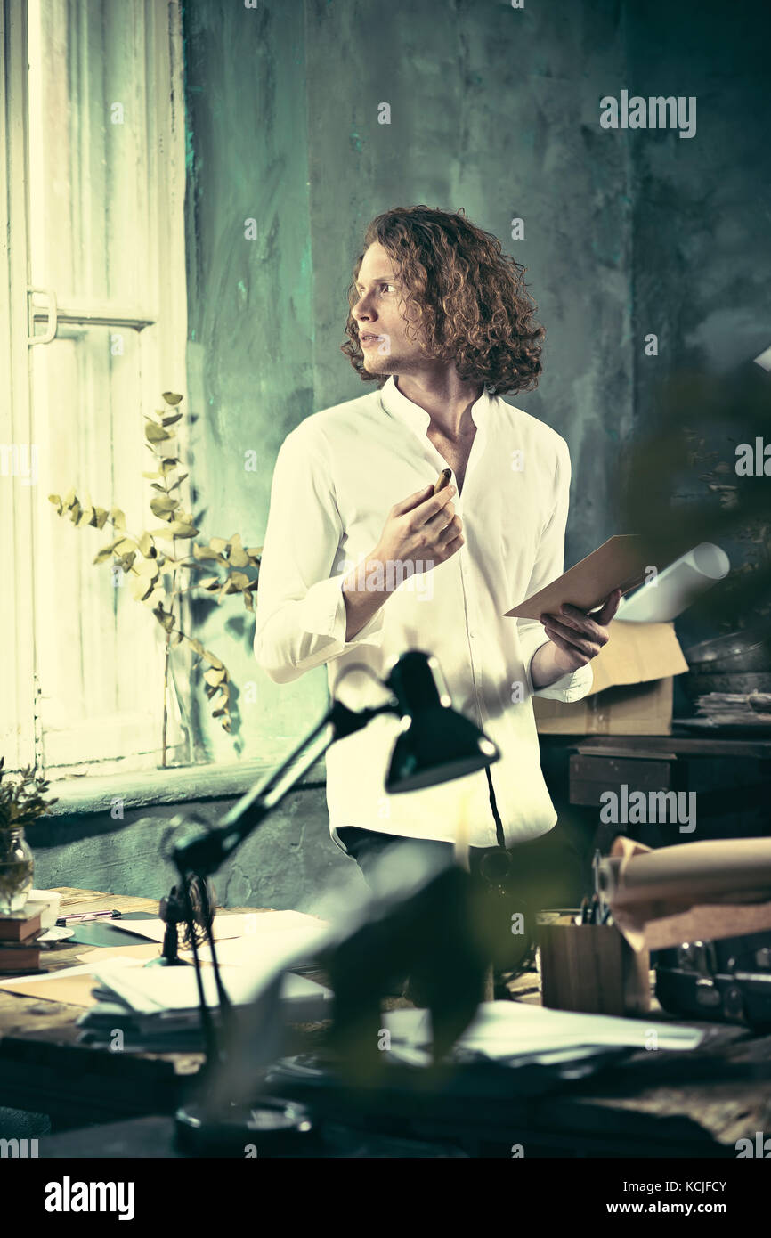 Writer at work. Handsome young writer standing near the table and ...