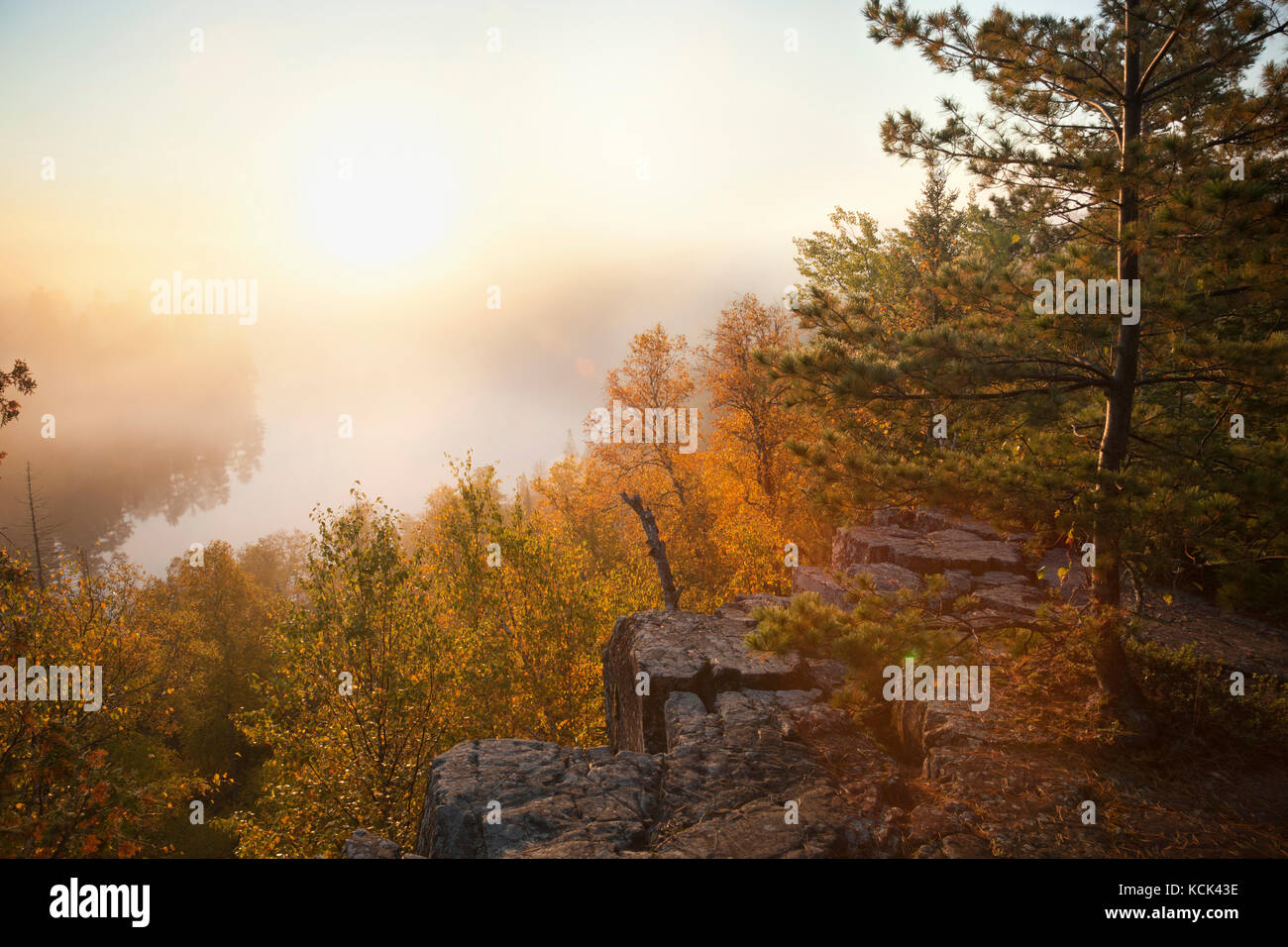 Granite cliff and pines overlooking misty lake in northern Minnesota ...