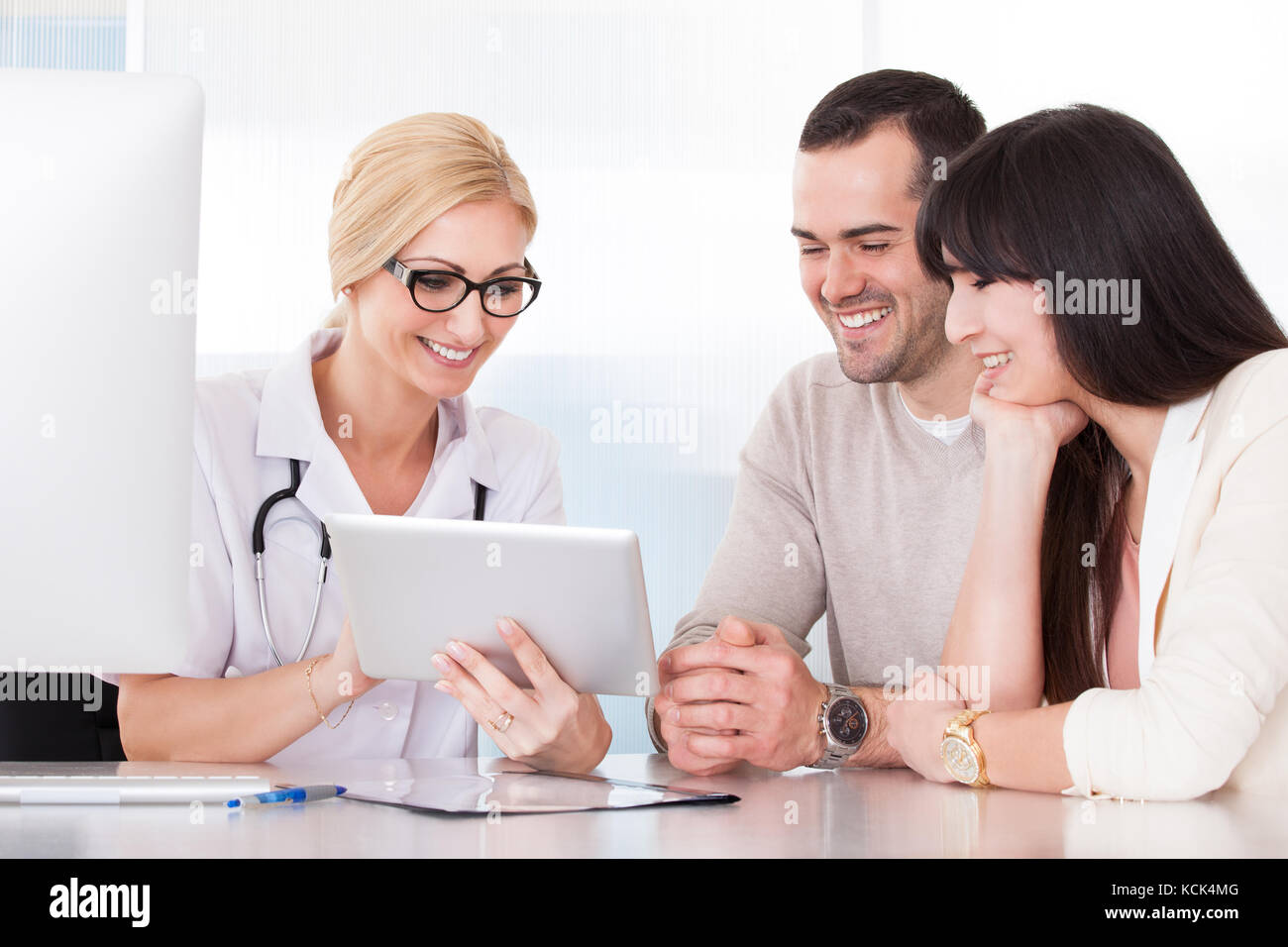 Happy Doctor Discussing With Couple In Clinic Stock Photo - Alamy