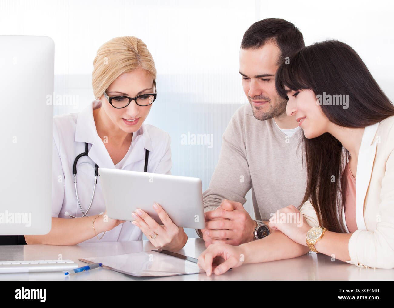 Happy Doctor Discussing With Couple In Clinic Stock Photo - Alamy