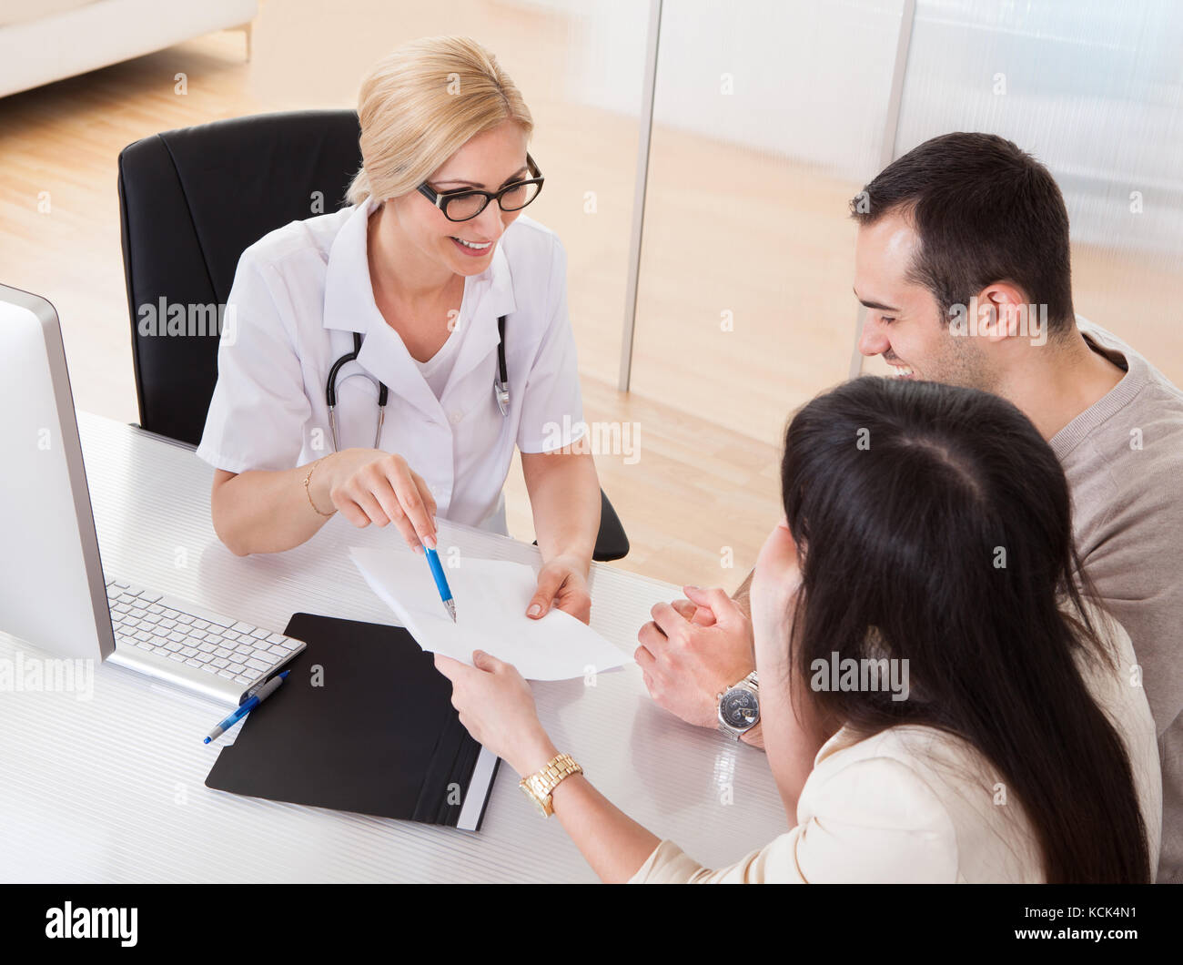 Happy Doctor Discussing With Couple In Clinic Stock Photo - Alamy