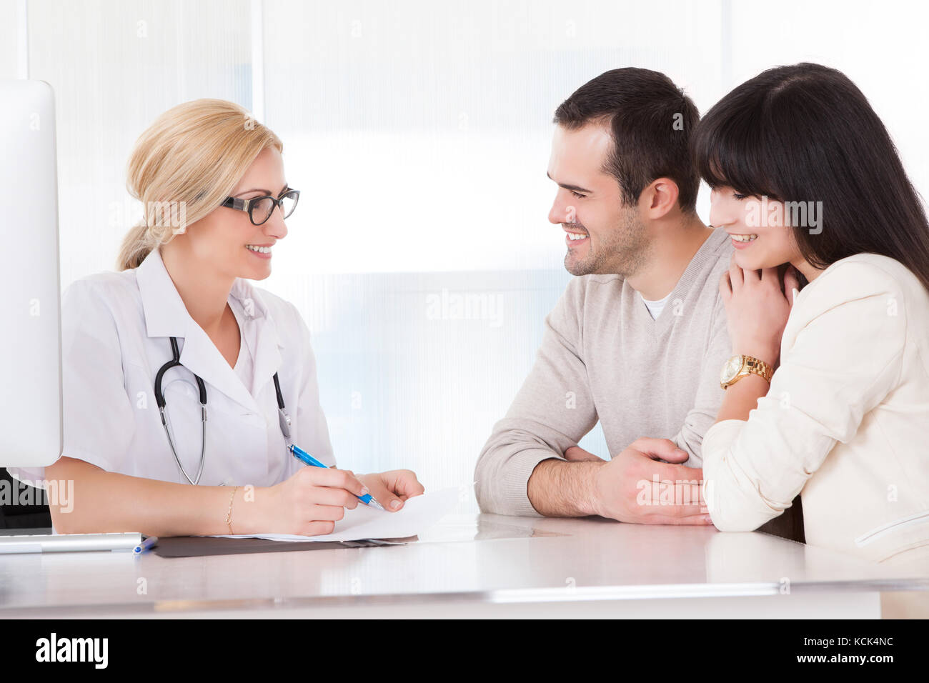 Happy Doctor Discussing With Couple In Clinic Stock Photo - Alamy