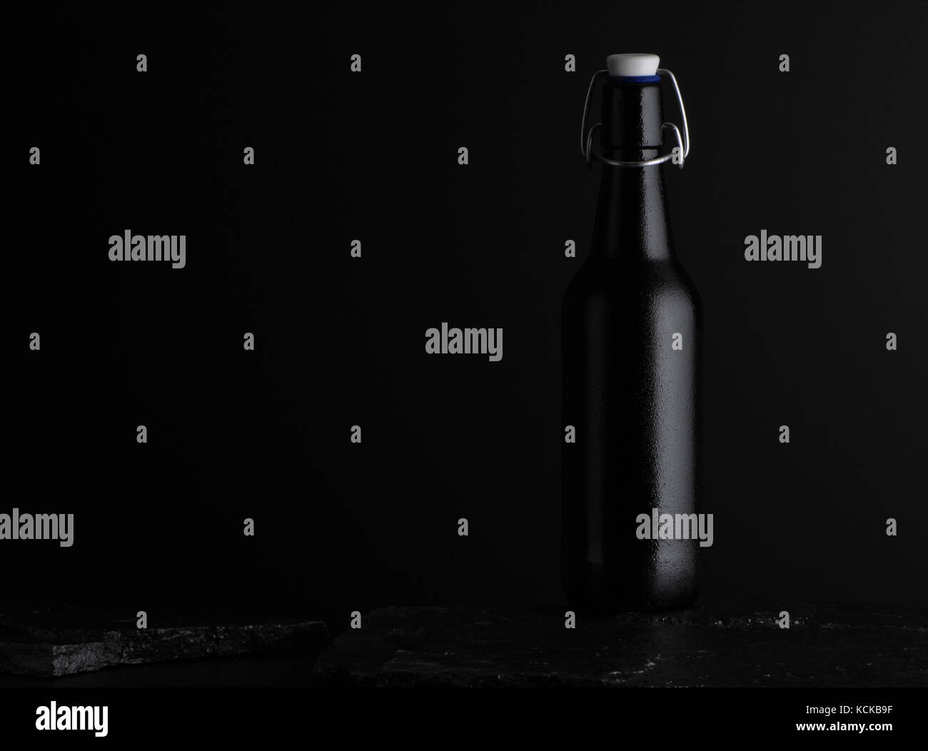 one sweating glass bottle with a cork on a rock on a dark background ...