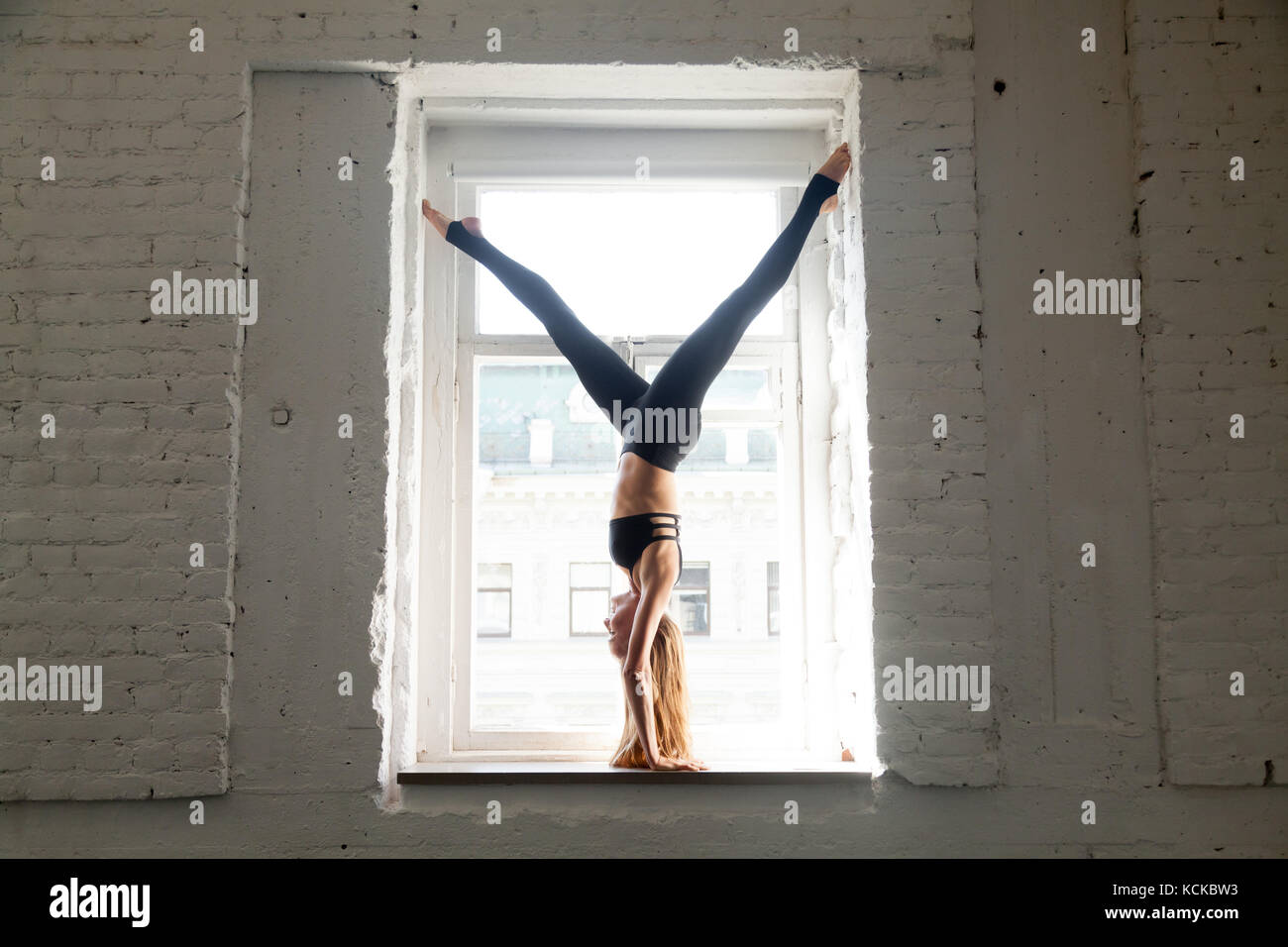 Young attractive woman practicing yoga, standing on window sill in Adho ...
