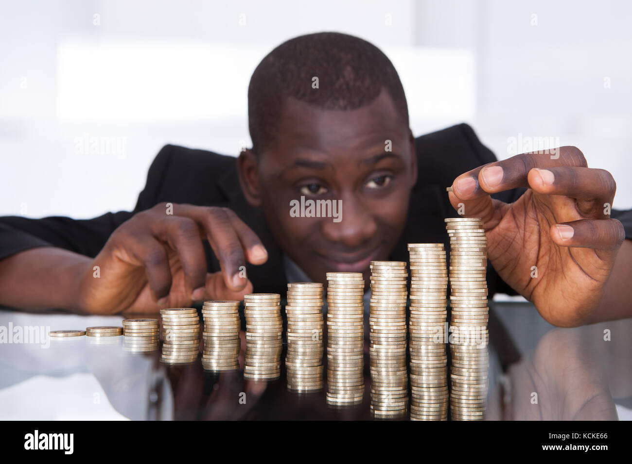 Portrait Of A Young African Businessman Stacking Coins In A Row On Desk ...