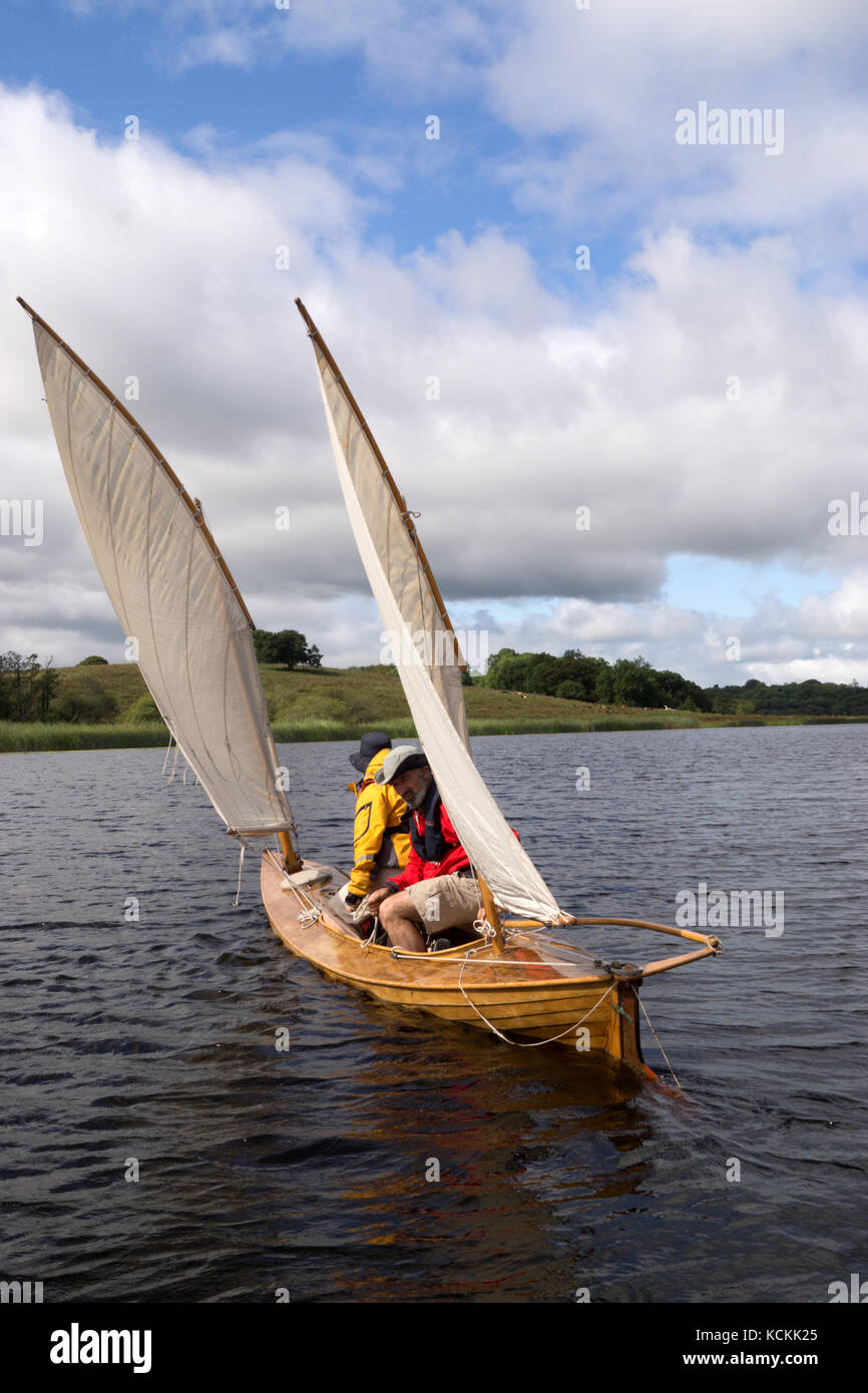 Wooden canoe on river, with two sails, sailing away with two men on ...
