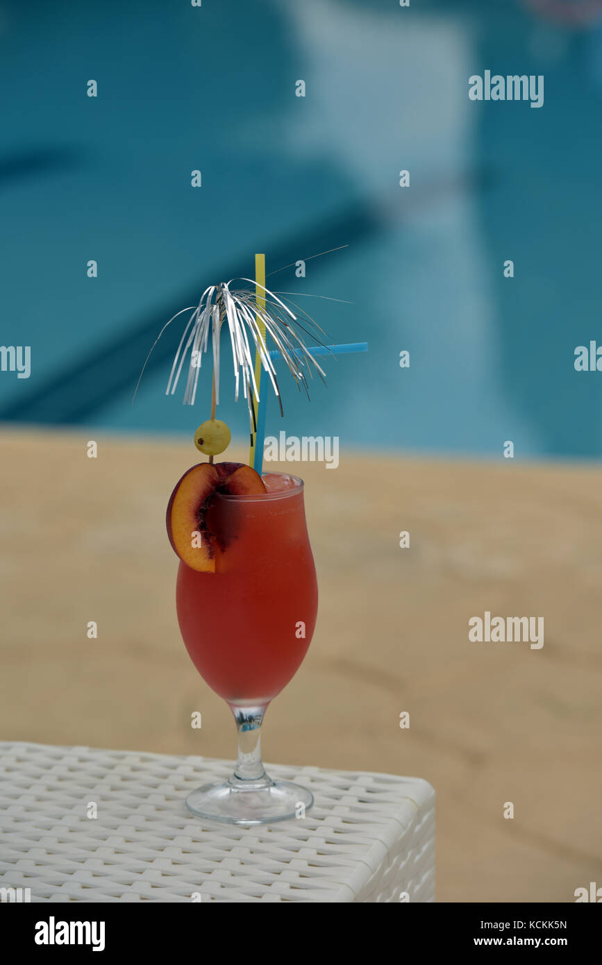 a colourful cocktail with straws and umbrella next to a swimming pool ...