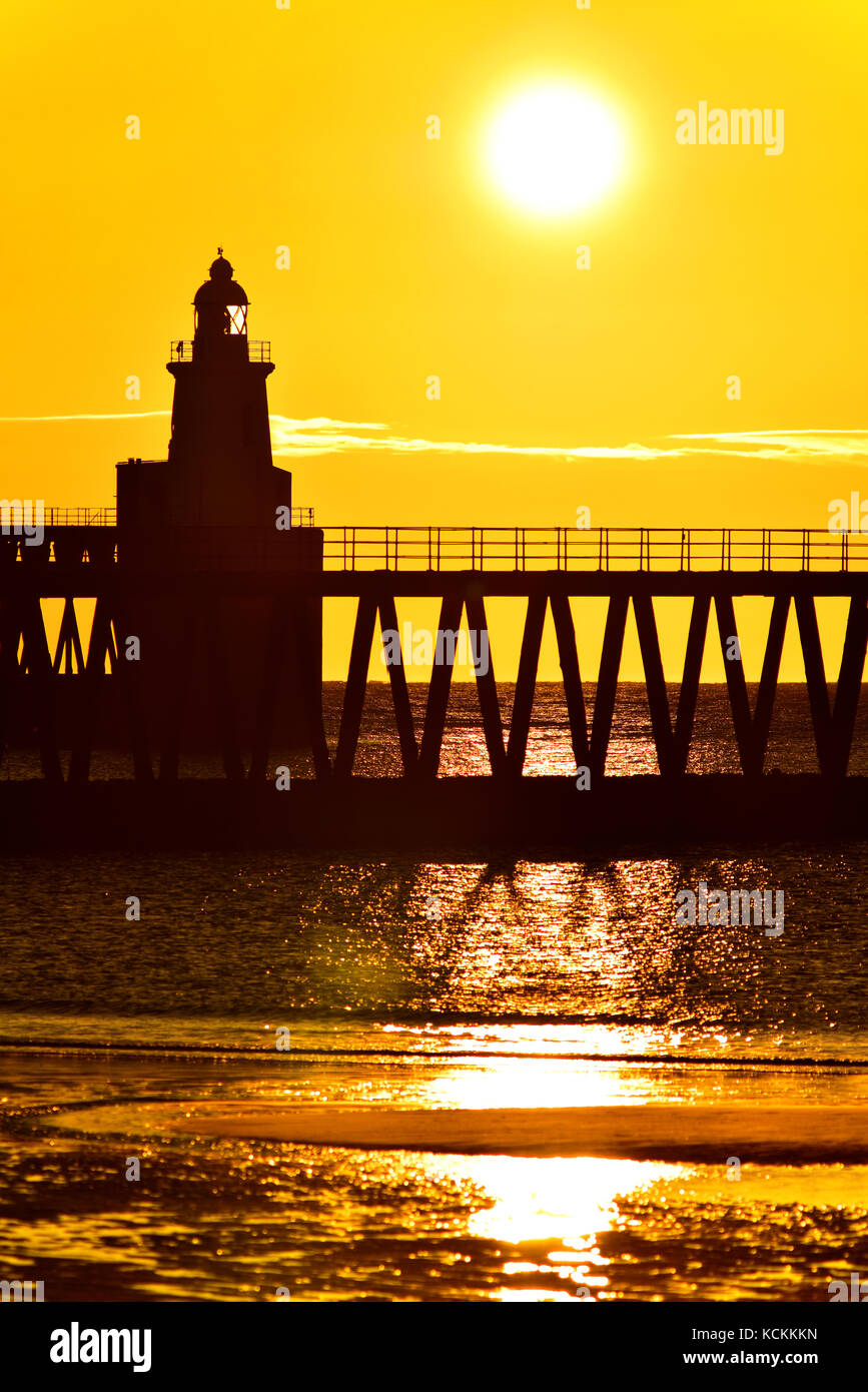 Blyth pier and lighthouse at sunrise with sun directly to the right of ...