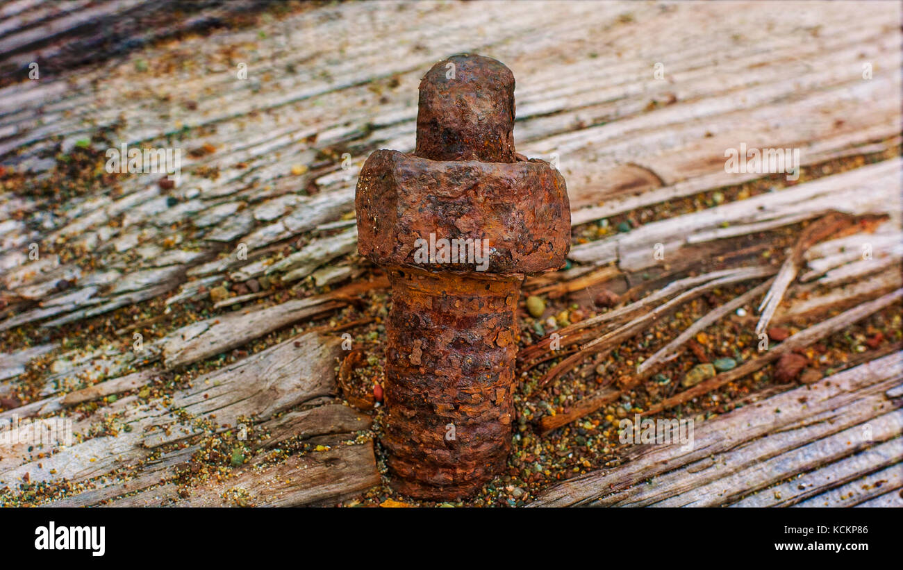 Rusted bolt and nut stuck in a weathered ships plank with sand and ...