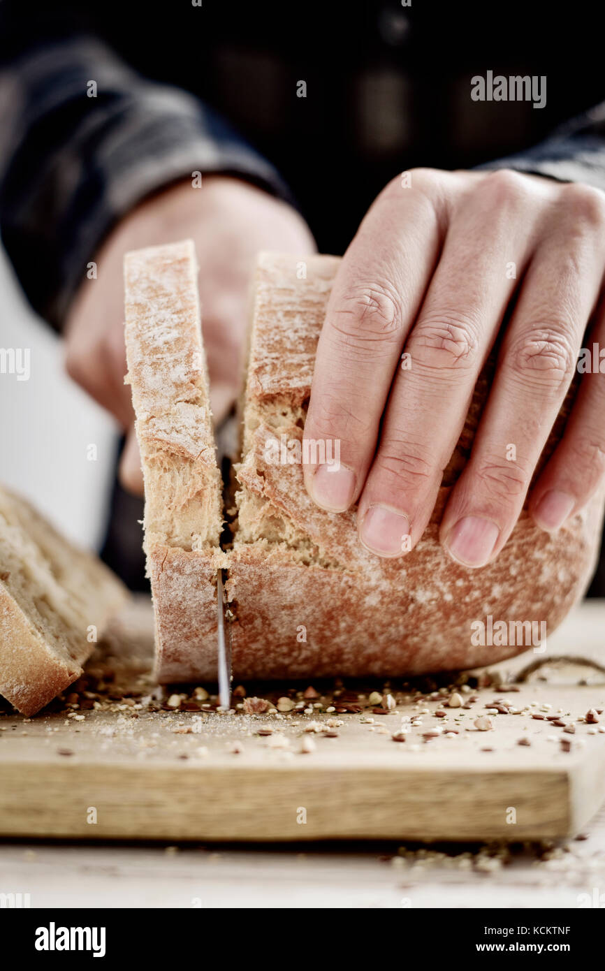 closeup of a young caucasian man cutting a spelt bread roll in slices ...