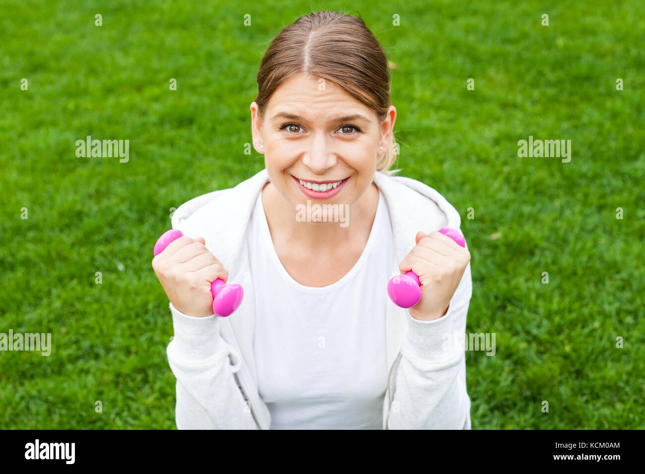 Young female doing fitness exercises with pink dumbbells in the park ...