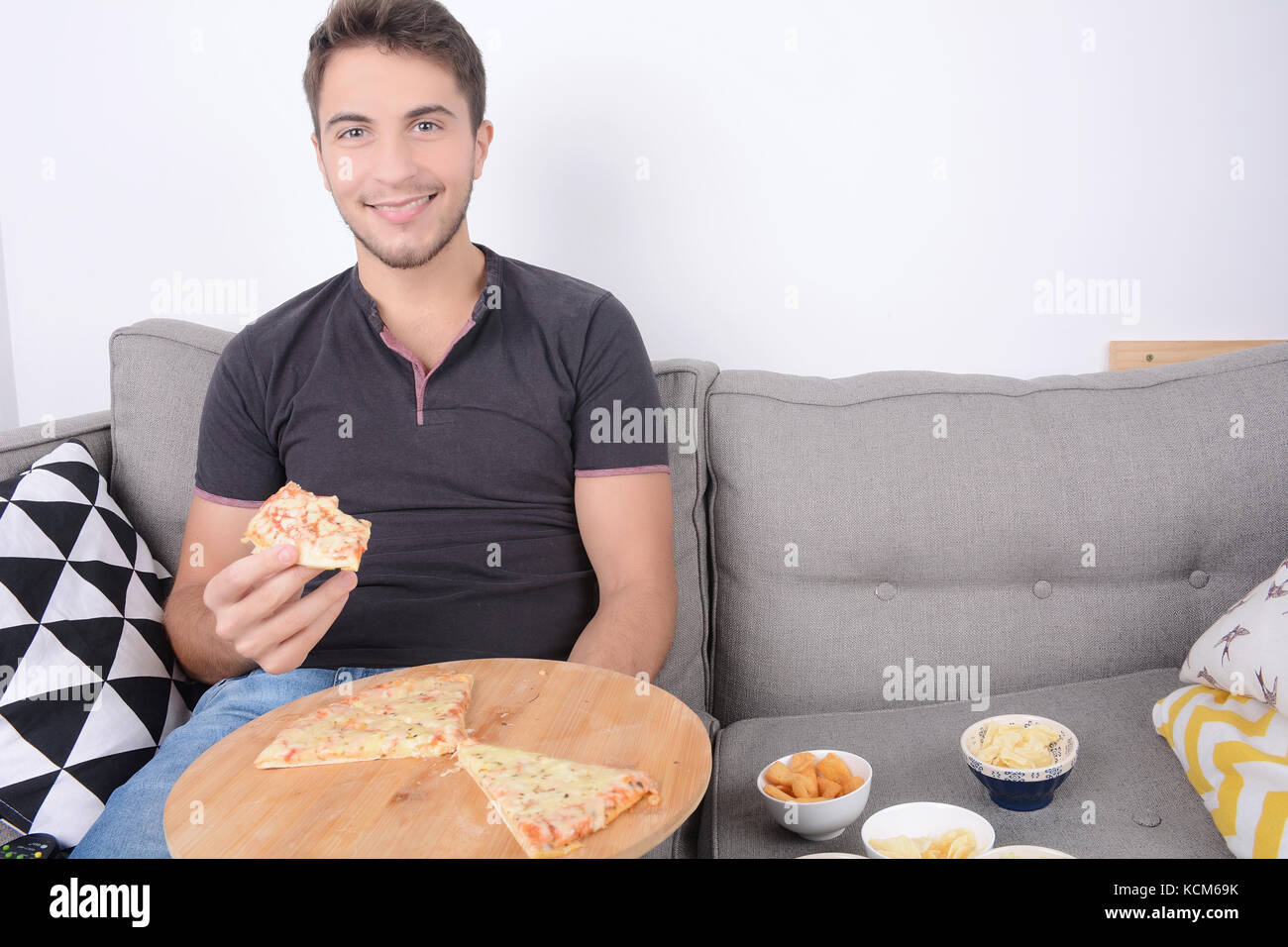 Attractive young man eating pizza on couch. Indoors Stock Photo - Alamy