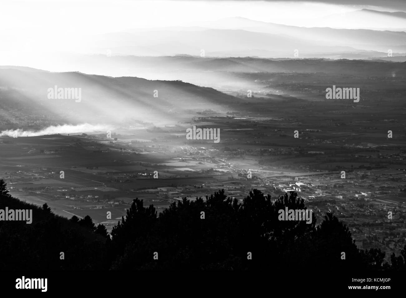 Aerial view of a valley, with sun rays coming out behind some mountains ...