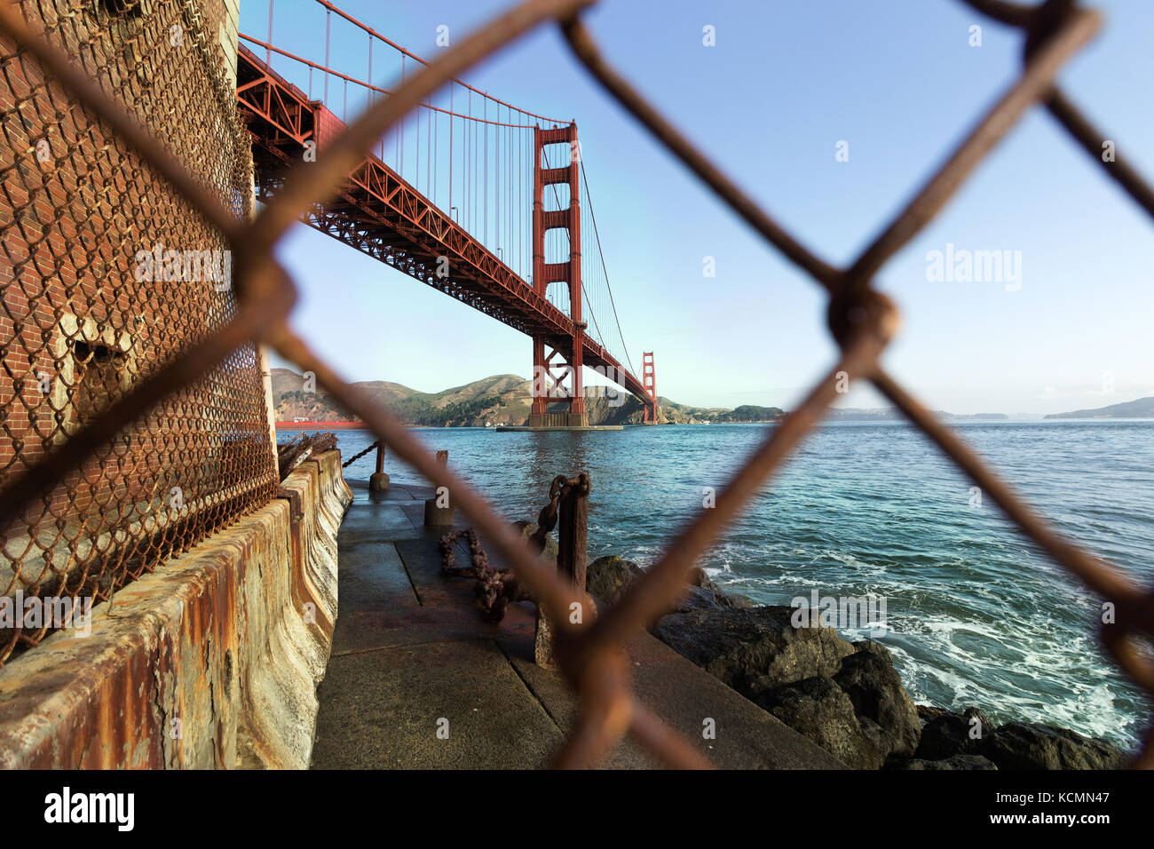 View through a wire fence of the Golden Gate Bridge at sunrise time ...