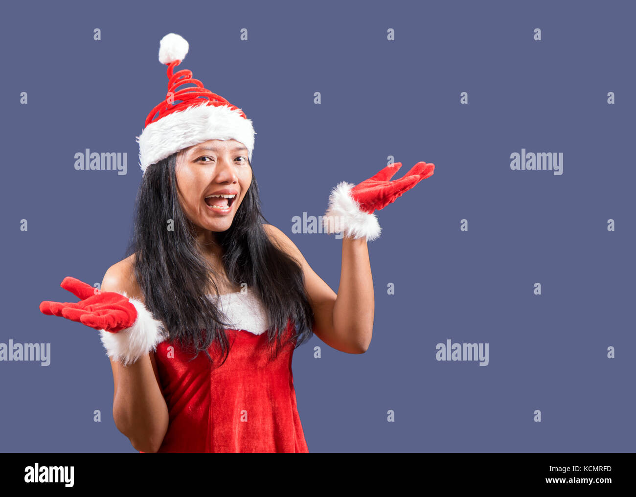 Funny cheerful Mrs. Claus looks to the camera with her hands up on blue ...
