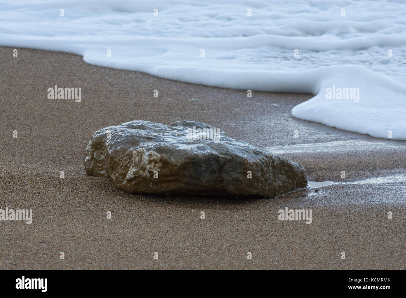 Single stone in surf on sandy beach, West Bay, Dorset, UK Stock Photo ...