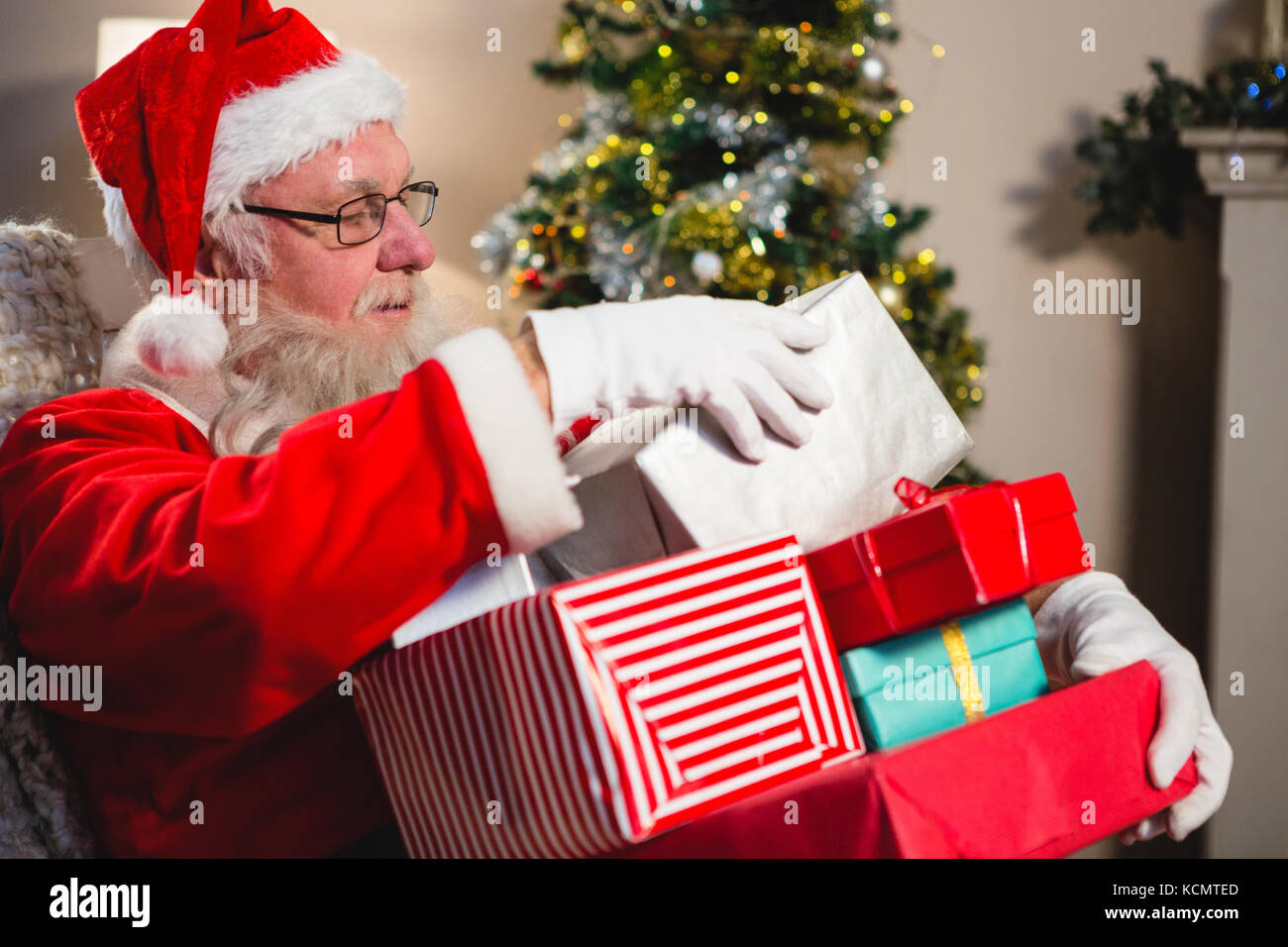 Santa claus sitting with stack of gift boxes in living room during ...