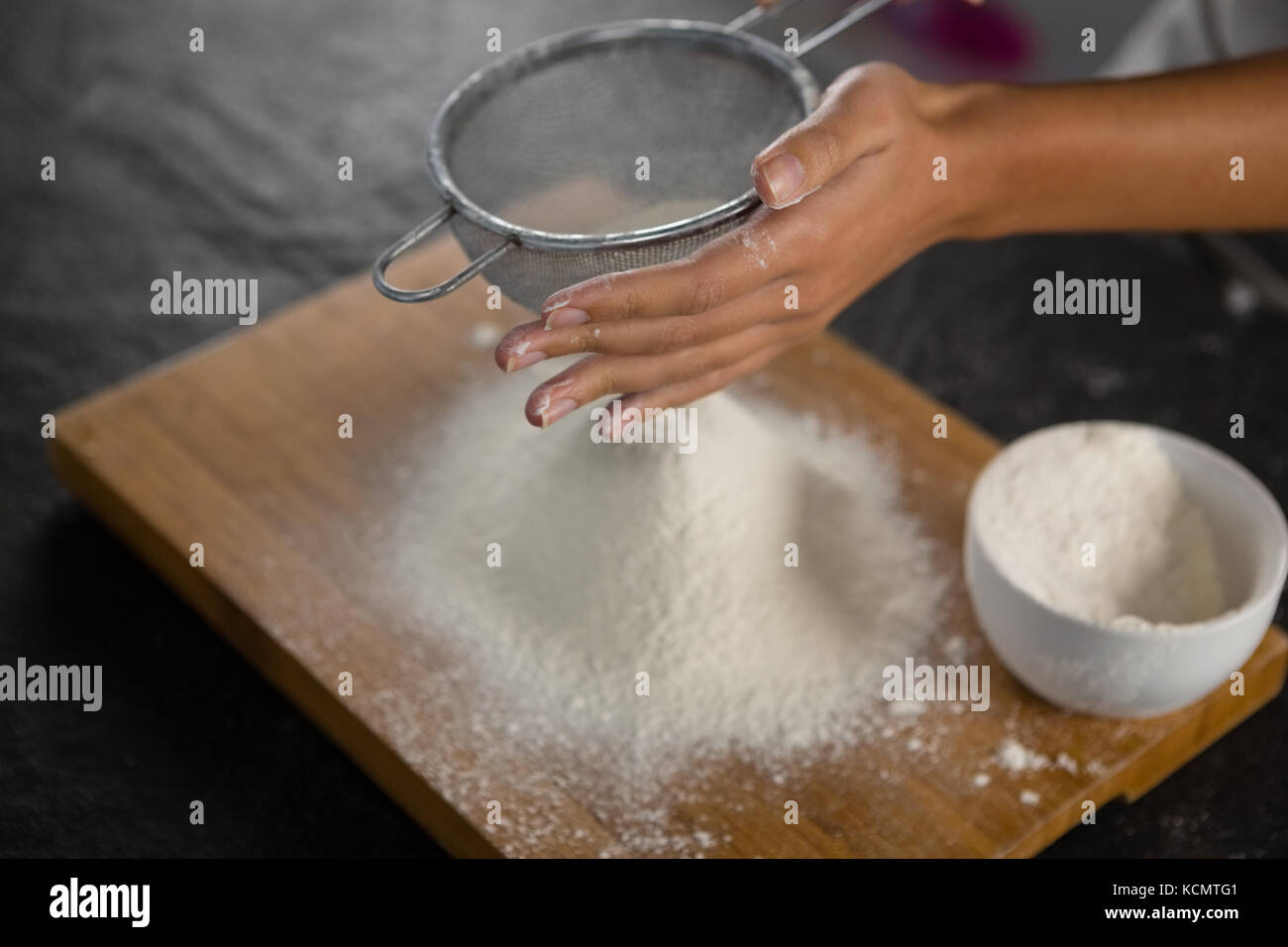 Close-up of woman sieving flour from the bowl on the wooden board Stock ...