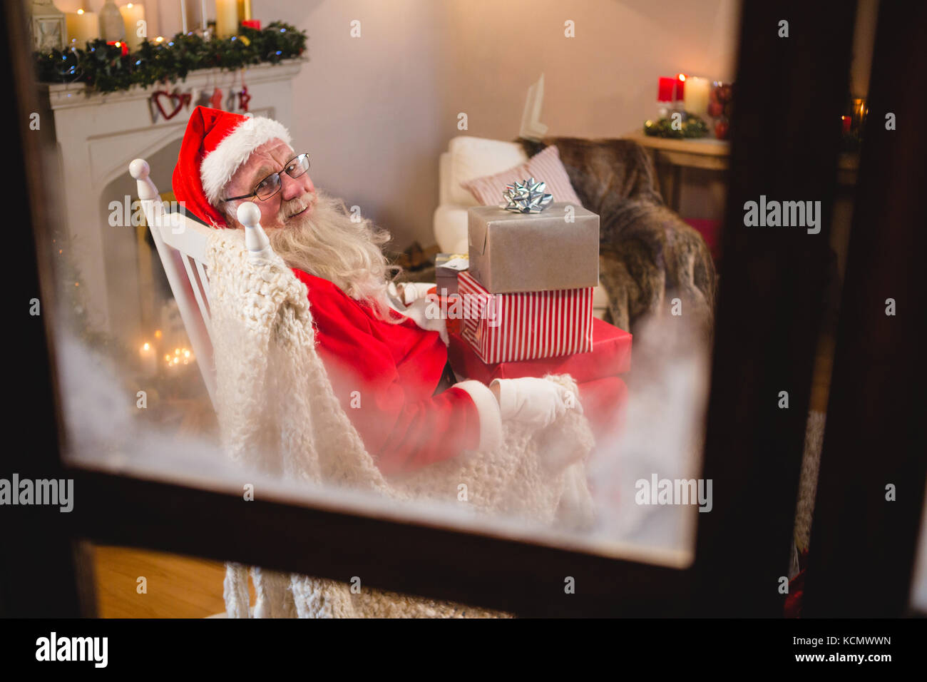 Portrait of santa claus sitting with stack of gift boxes in living room ...