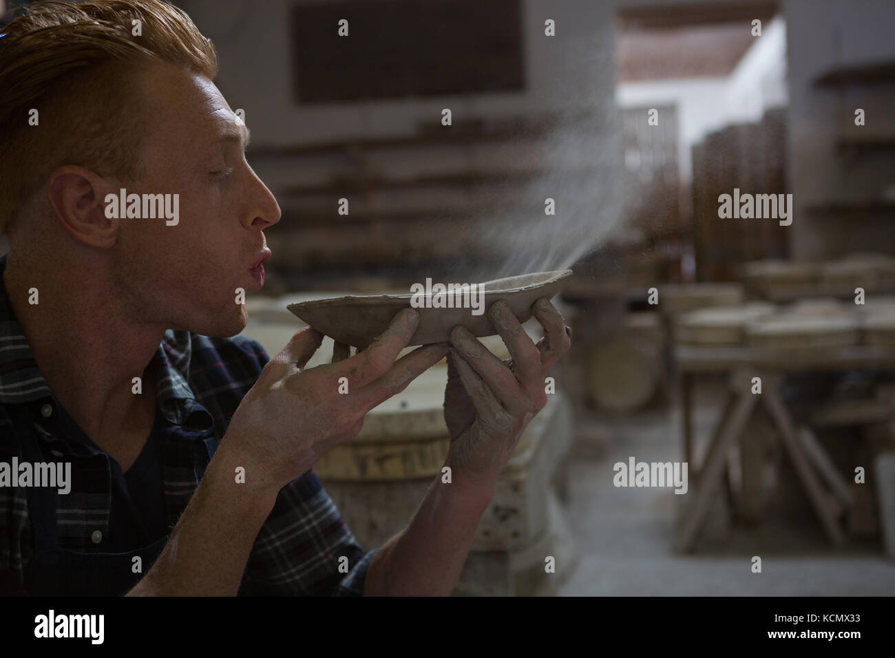 Male potter blowing dust from a bowl in pottery workshop Stock Photo ...