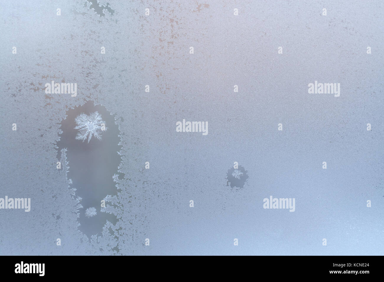 Frosty winter window glass, two thawed spots with snowflakes inside and ...