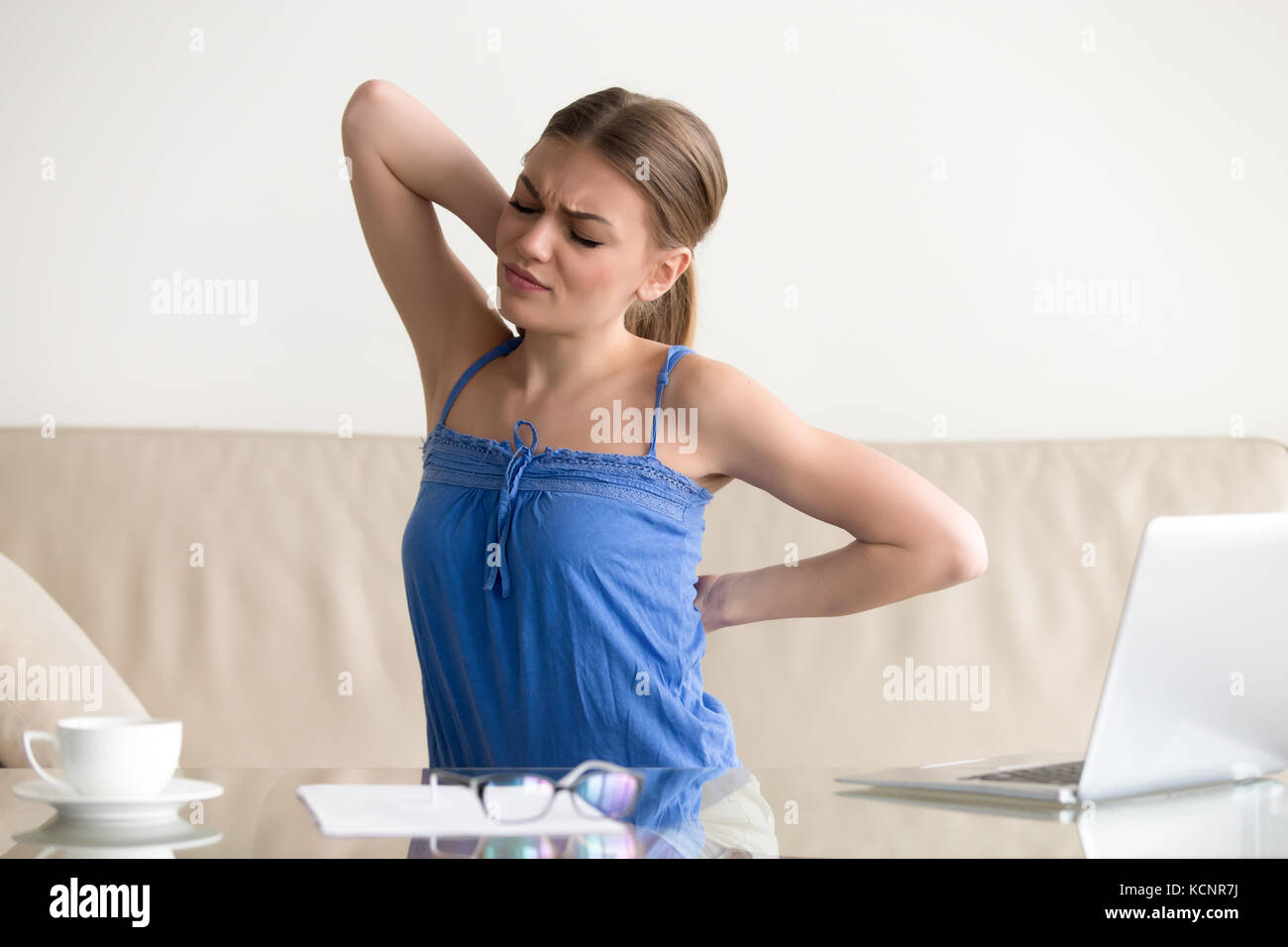 Young woman stretching suffering from sudden back pain, tensed muscles ...