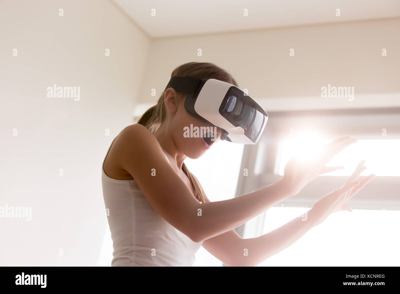 Shocked girl looking at her own hands through virtual reality goggles ...