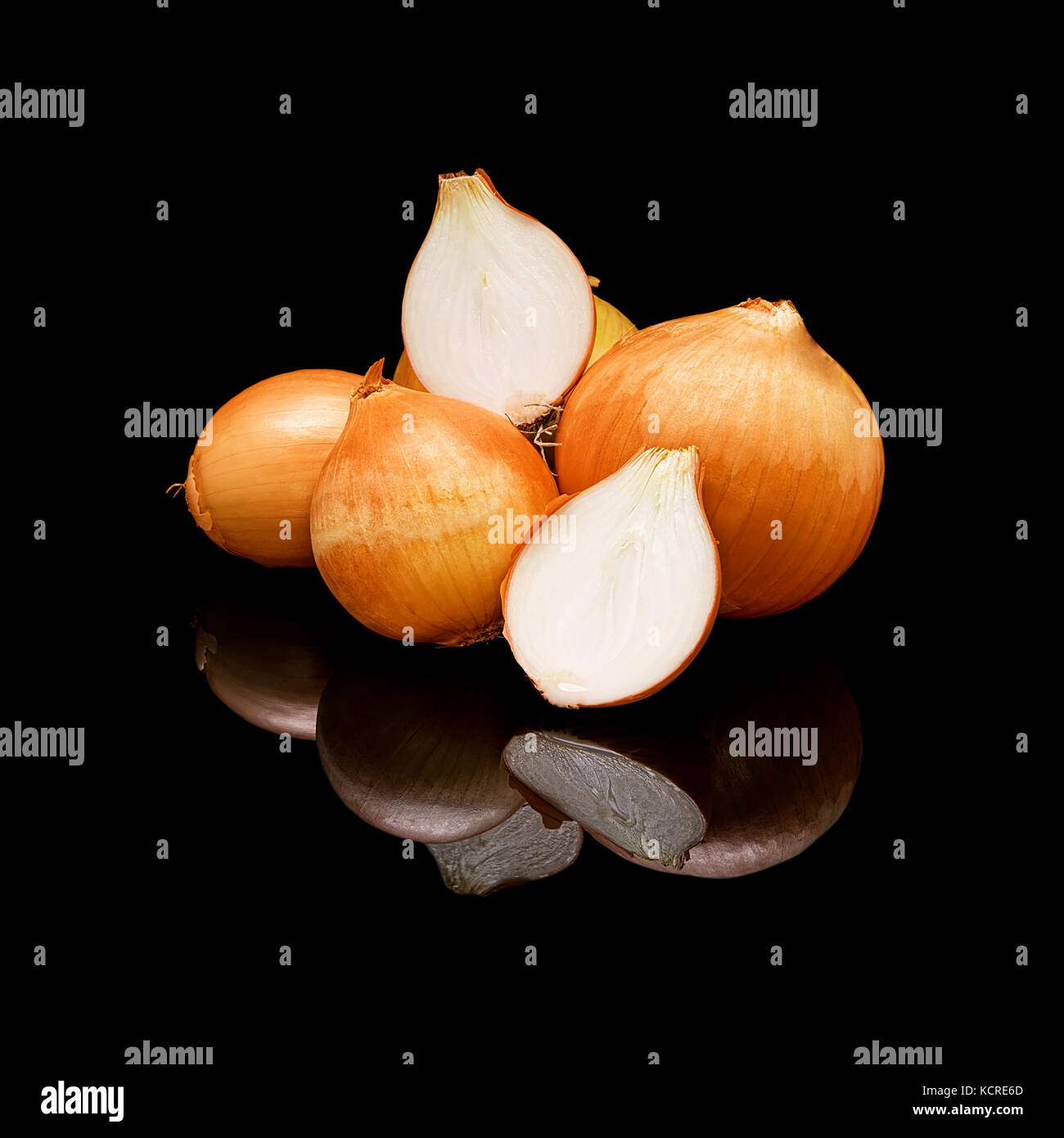 Pile of whole and cut onions with golden skin. On a black glossy ...