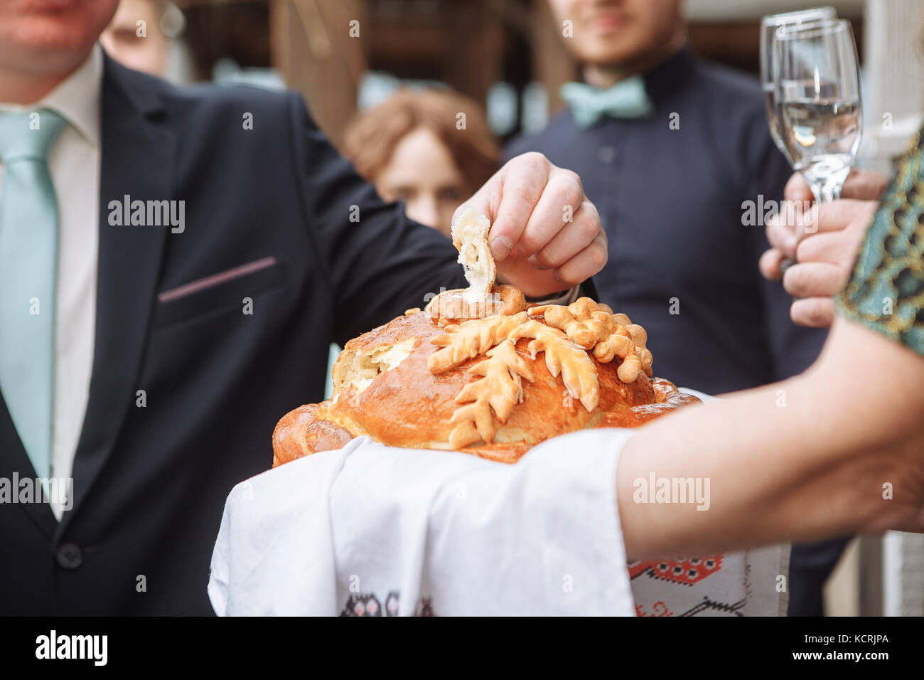Groom holding slice of traditional wedding round loaf and bride salt it ...