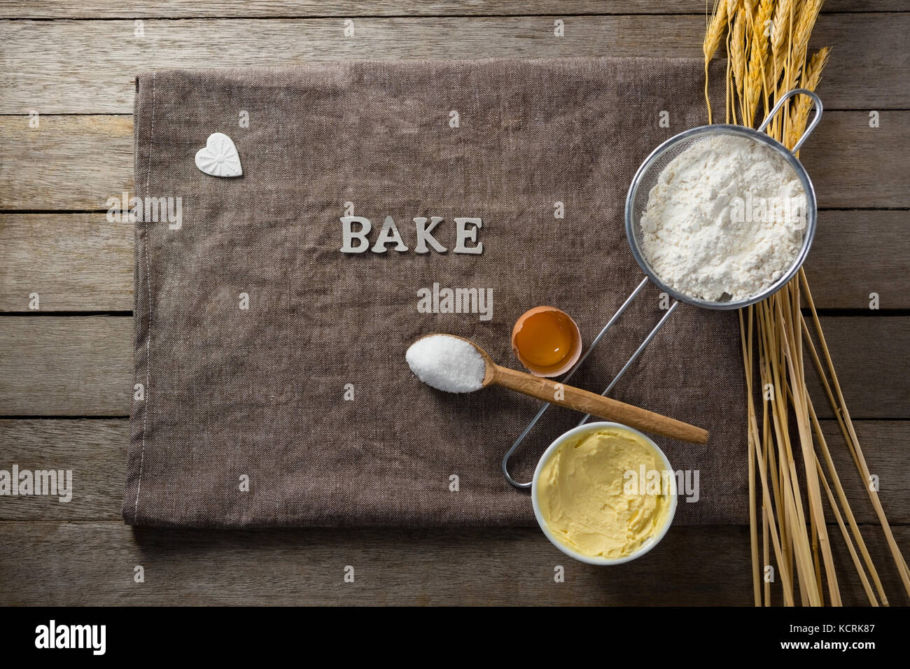 Over head view of wheat stem, wear flour, sieve, spoon placed over a ...